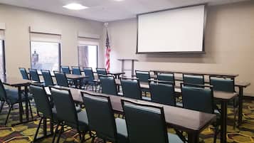 Uma sala de conferências com fileiras de cadeiras e mesas, uma bandeira americana e uma tela de projeção.