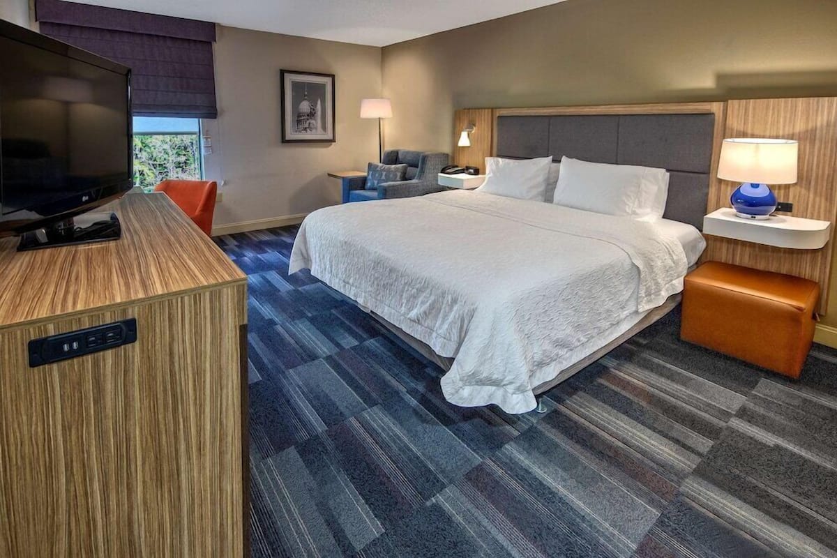 Quarto de hotel com uma cama grande, televisão, escrivaninha e uma cadeira.