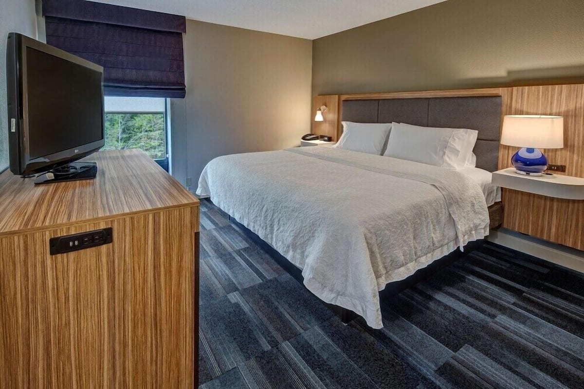Quarto de hotel com cama, televisão, escrivaninha e janela com vista.