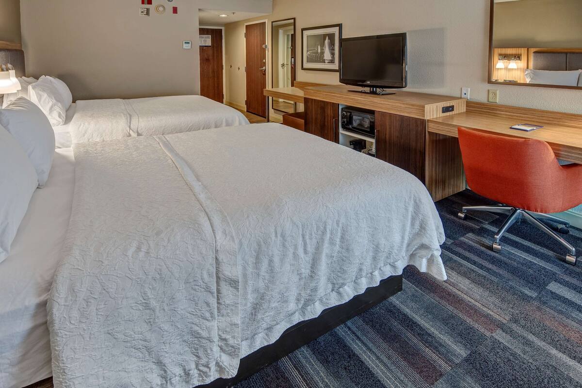 Quarto de hotel com duas camas, uma escrivaninha com televisão e uma cadeira.