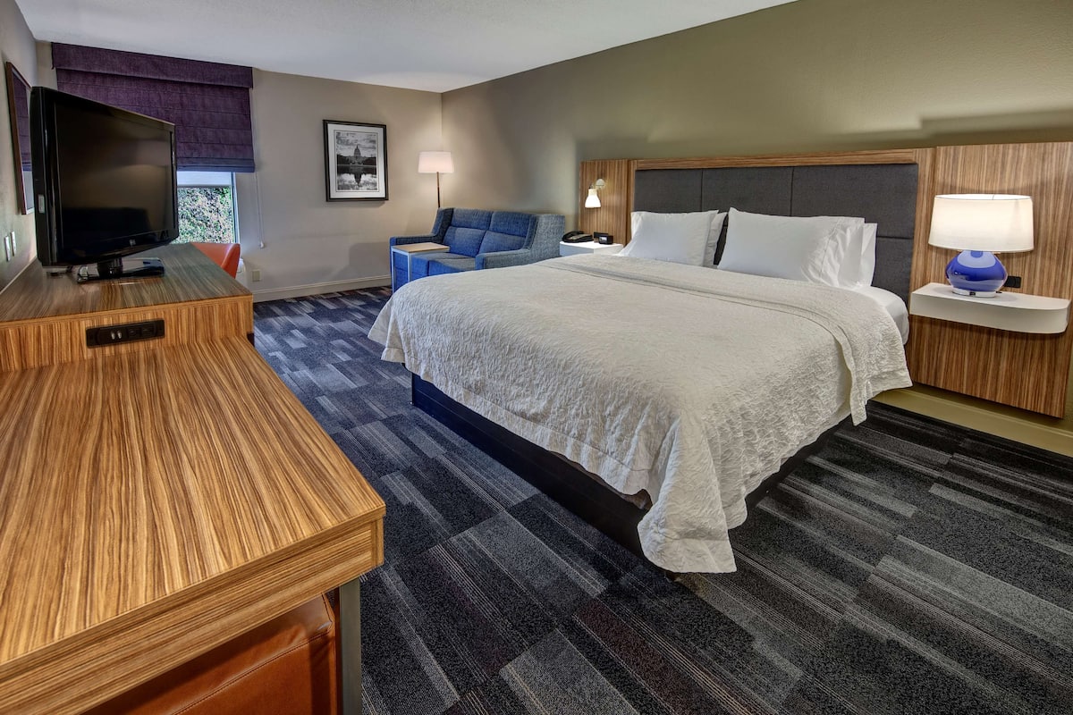 Quarto de hotel com uma cama grande, televisão, escrivaninha e uma cadeira.