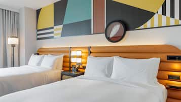 Quarto de hotel com duas camas, cabeceira com iluminação integrada, mesa de cabeceira com abajur e uma obra de arte na parede.