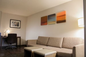 Quarto de hotel com sofá, uma secretária com cadeira e uma lâmpada. Três quadros na parede.