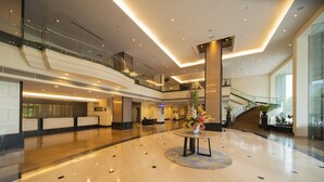 Um hall amplo com uma mesa de recepção, escadaria e um arranjo de plantas decorativo.