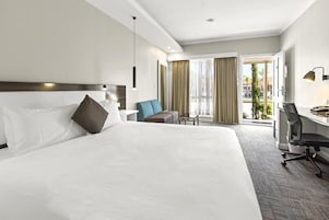 Quarto de hotel com uma cama grande, uma escrivaninha, uma cadeira e vista para o exterior através de uma porta.
