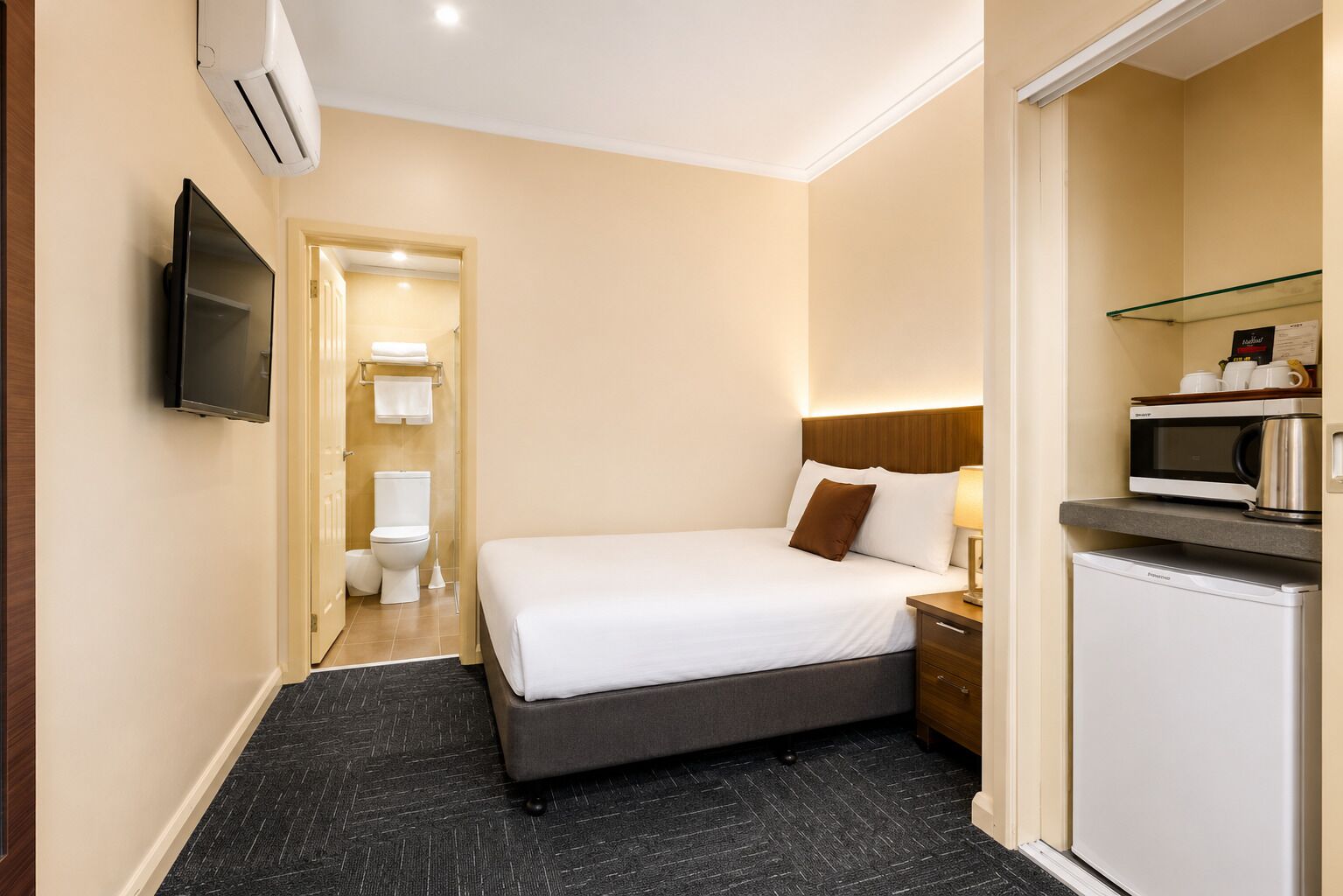 Quarto de hotel com cama, mesa de cabeceira, televisão, micro-ondas e mini-geladeira.