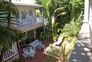 Um edifício de dois andares com varanda, área de estar ao ar livre e plantas tropicais exuberantes.