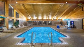 Piscina interna com vigas de madeira, espreguiçadeiras e máquina de refrigerantes Pepsi.