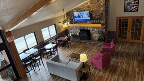 Um quarto espaçoso com lareira de pedra, piso de madeira, televisão na parede e um espaço de estar com sofá e poltronas.