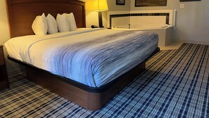 Quarto de hotel com uma cama grande, banheiro com banheira e mesa de cabeceira.