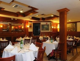 Restaurante com mesas redondas, cadeiras de madeira e uma estante para vinhos na parede.