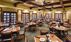 Um restaurante espaçoso com várias mesas e cadeiras, janelas amplas e ventiladores de teto.
