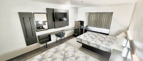 Quarto de hotel com duas camas, uma mesa, uma televisão e uma janela com cortinas.