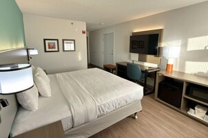 Quarto de hotel com cama, escrivaninha, cadeira, televisão e um pequeno espaço de estar.
