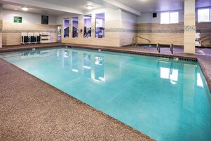 Piscina interior com água cristalina, placa indicando proibição de mergulhos e área de vestiários.