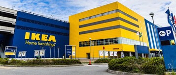 Um edifício grande e moderno com fachada destacada em amarelo e azul, exibindo o logotipo da IKEA e sinalização para artigos de casa.