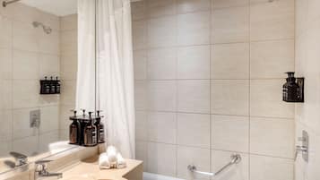 Um banheiro moderno com parede revestida de azulejos bege, pia com espelho, chuveiro com cortina e duas garrafas de shampoo na parede.