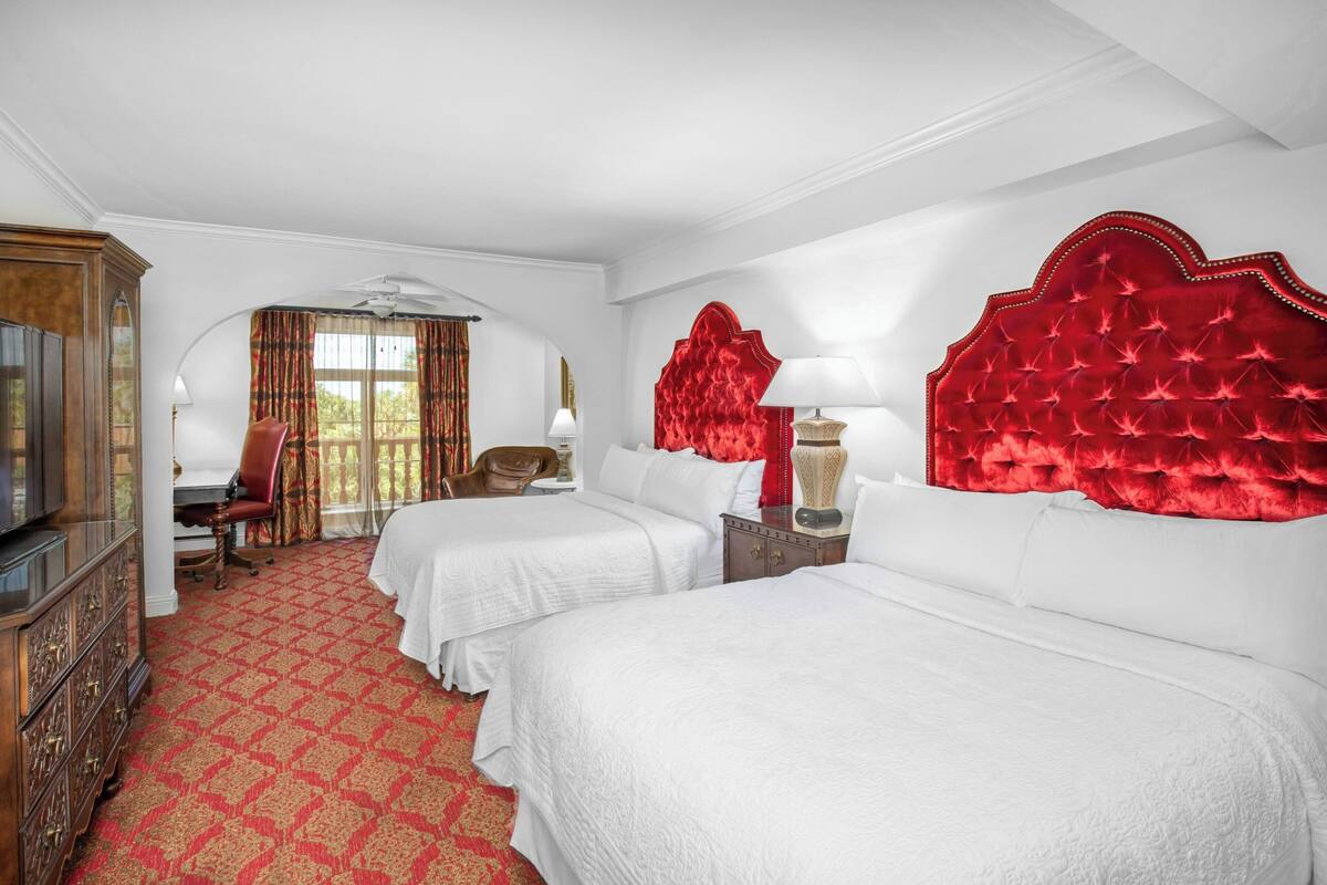 Quarto de hotel com duas camas, uma escrivaninha, uma cadeira e um guarda-roupa.