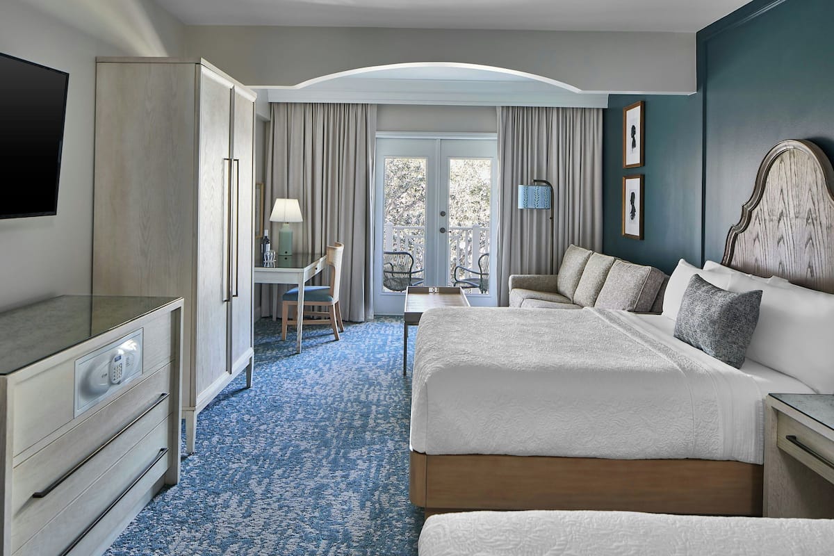 Quarto de hotel com uma cama grande, uma escrivaninha e uma cadeira. Possui uma varanda com vista para árvores.