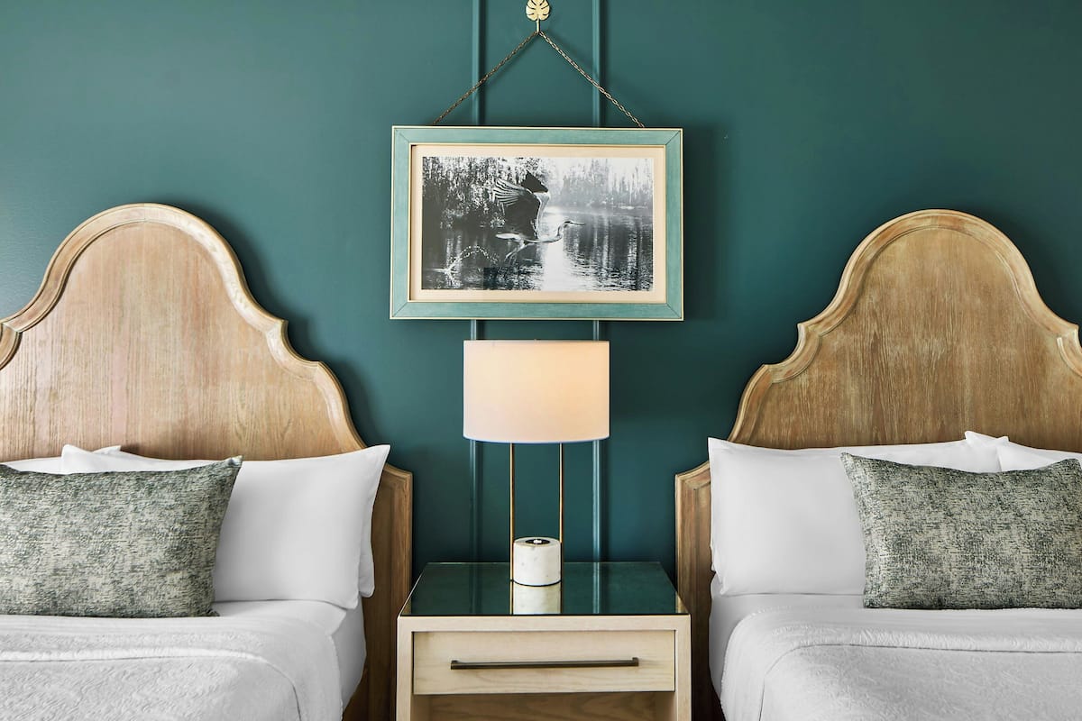 Quarto com duas cabeceiras de madeira, uma mesa de cabeceira com abajur e um quadro na parede.