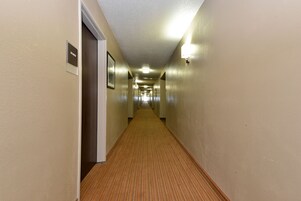 Um corredor comprido e estreito com piso coberto por carpete e paredes em tom claro.