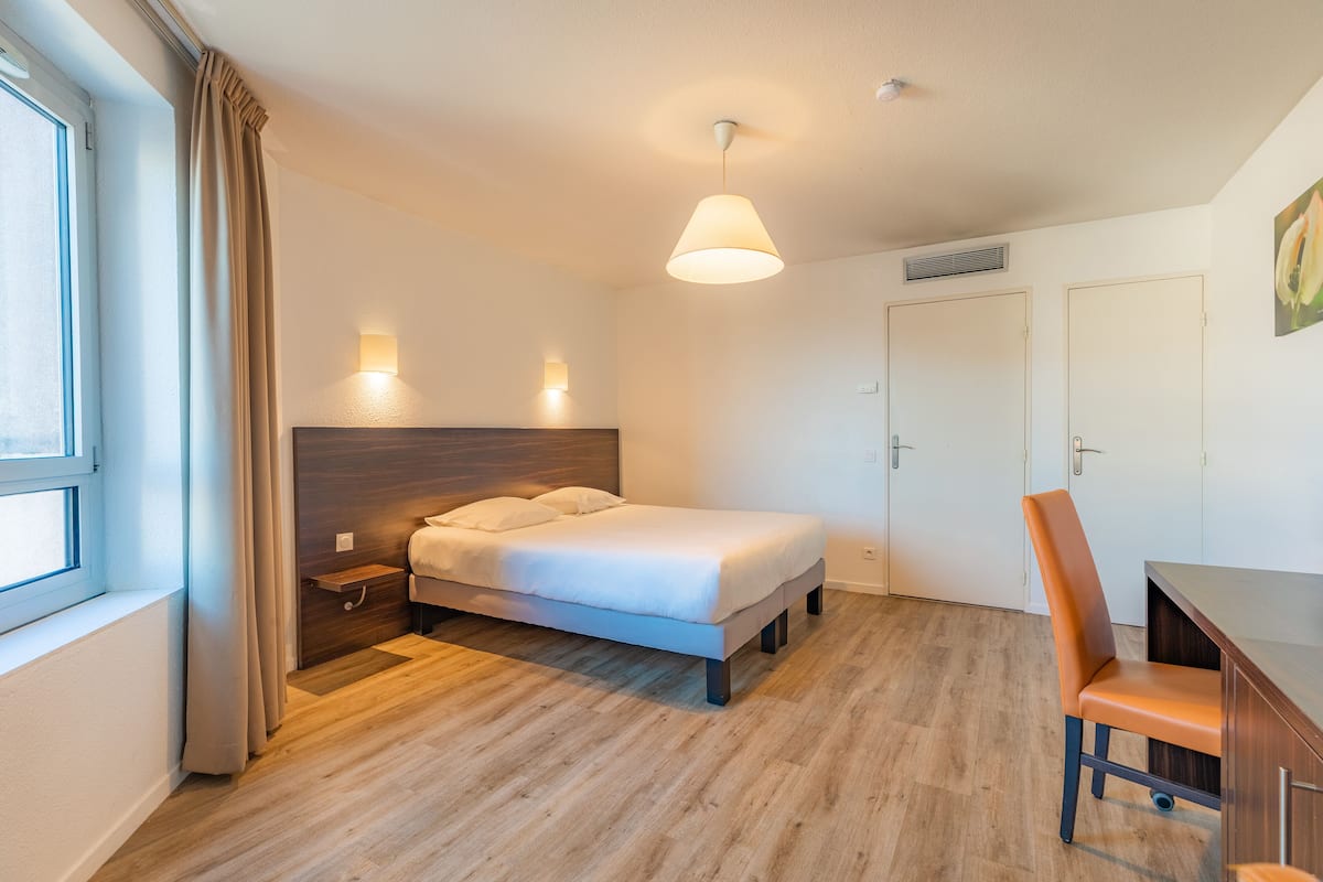 Quarto com cama, mesa de cabeceira, luminária, cadeira e escrivaninha.