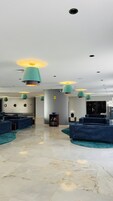 Um hall amplo com luminárias pendentes verde-água, piso de mármore e áreas de estar em azul.