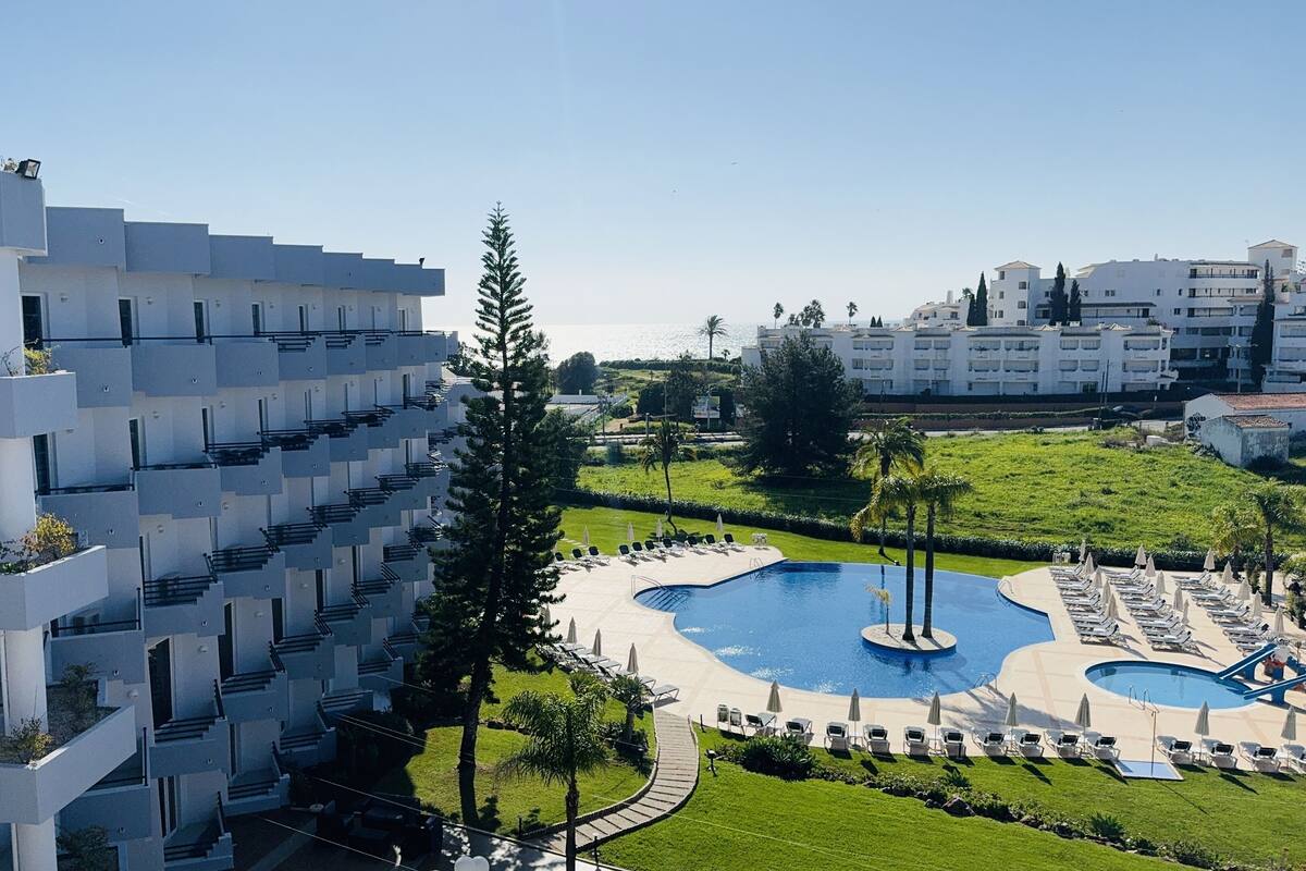 Um hotel moderno com área de piscina, incluindo uma fonte central e espreguiçadeiras.