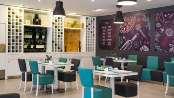 Interior de restaurante moderno com cadeiras brancas e azul-turquesa, luminárias pendentes pretas e parede com ilustrações de comida.