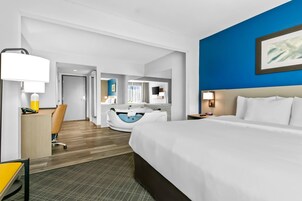Quarto de hotel moderno com uma cama grande, uma escrivaninha com cadeira, uma toucador com espelho e uma banheira.