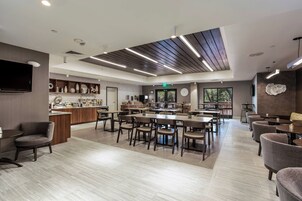 Um restaurante espaçoso com várias mesas e cadeiras, uma área de cozinha e um design de teto moderno.