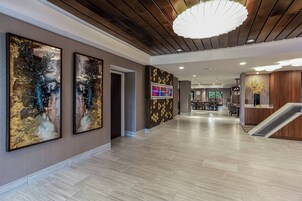 Um saguão de hotel moderno com tetos de painel de madeira, uma escadaria central e grandes pinturas abstratas nas paredes.