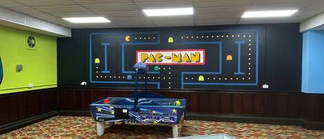 Quarto com mesa de futebol de mesa, parede com tema Pac-Man e carpete estampado.