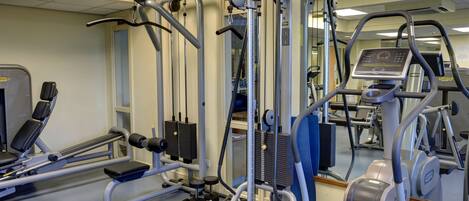 Uma academia com diversos equipamentos de exercício, incluindo esteiras, máquinas de musculação e pesos livres.