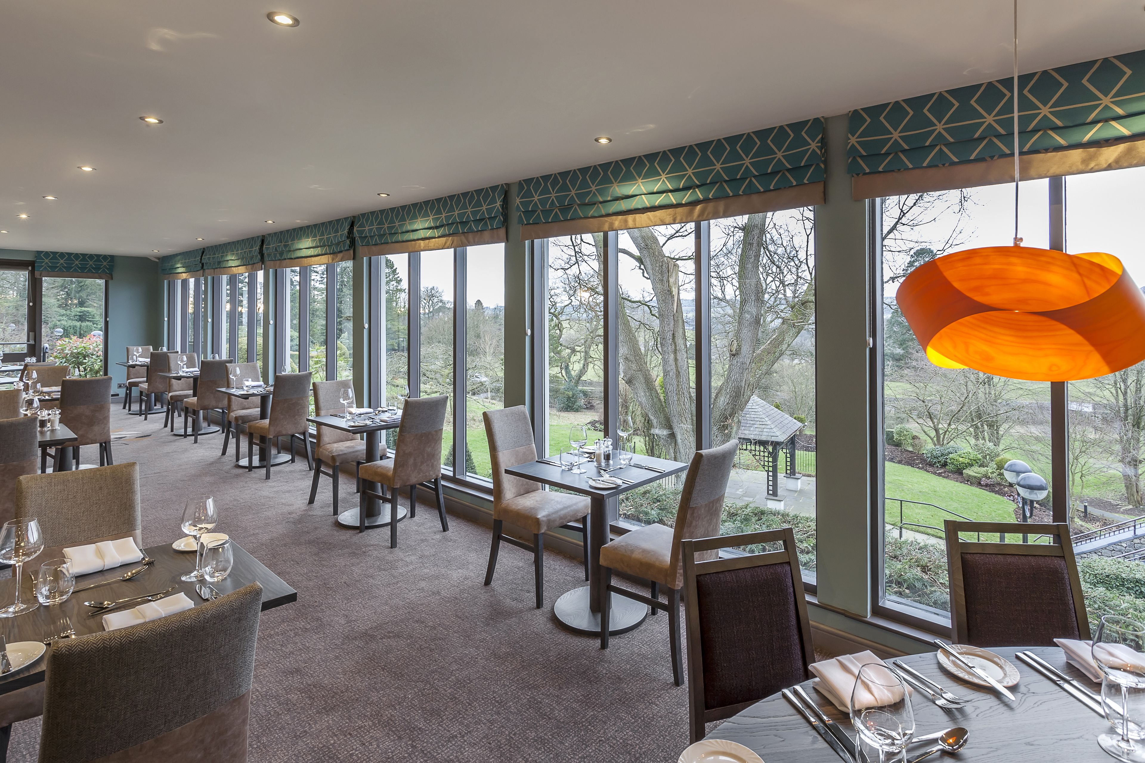 Restaurante com mesas preparadas para refeições, amplas janelas com vista para o exterior e uma luminária pendente.