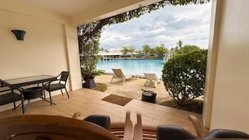 Um pátio com mesa e cadeiras, vista para uma piscina e espreguiçadeiras.