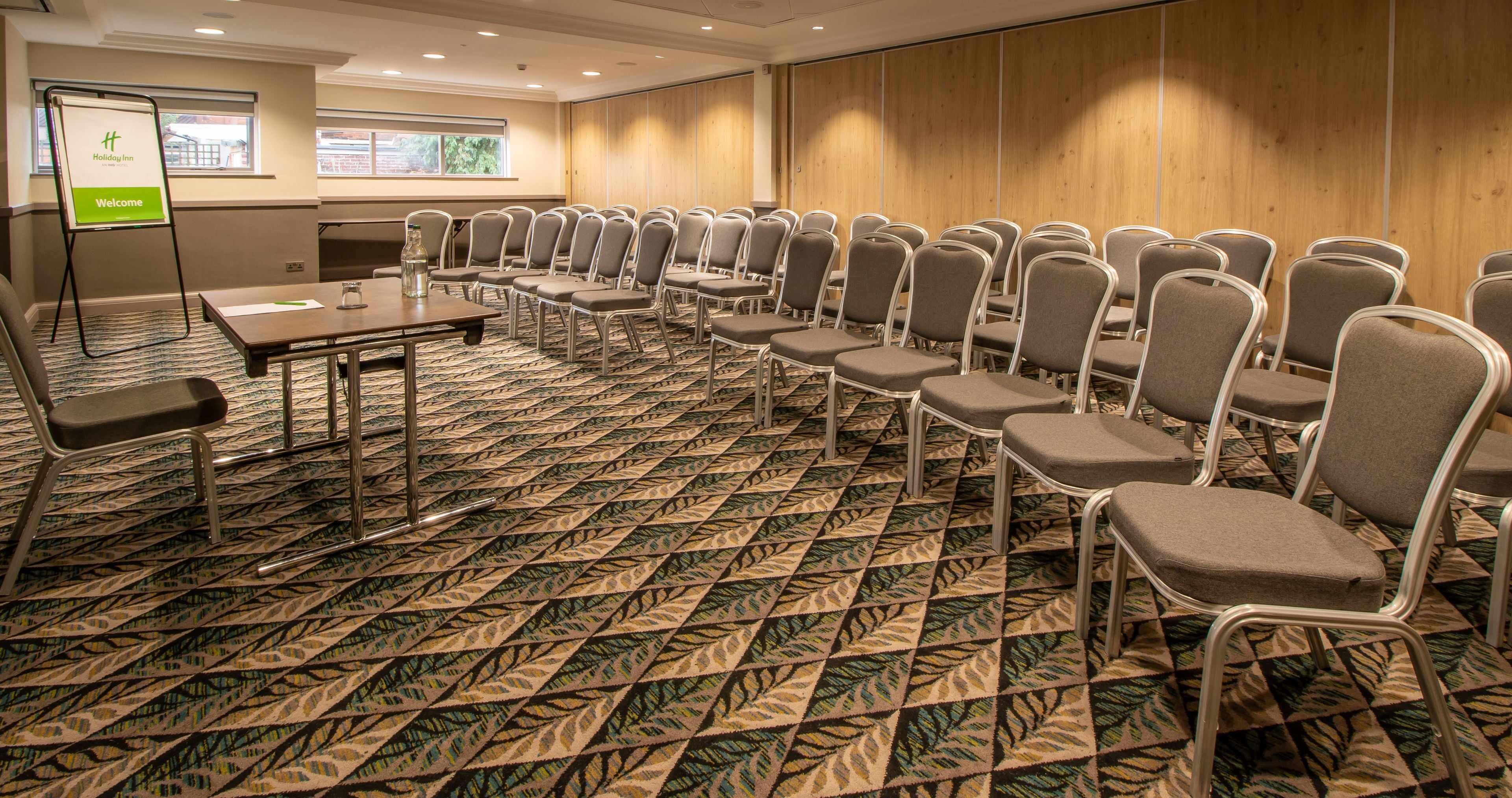 Uma sala de conferências com fileiras de cadeiras, uma mesa e um letreiro de boas-vindas.