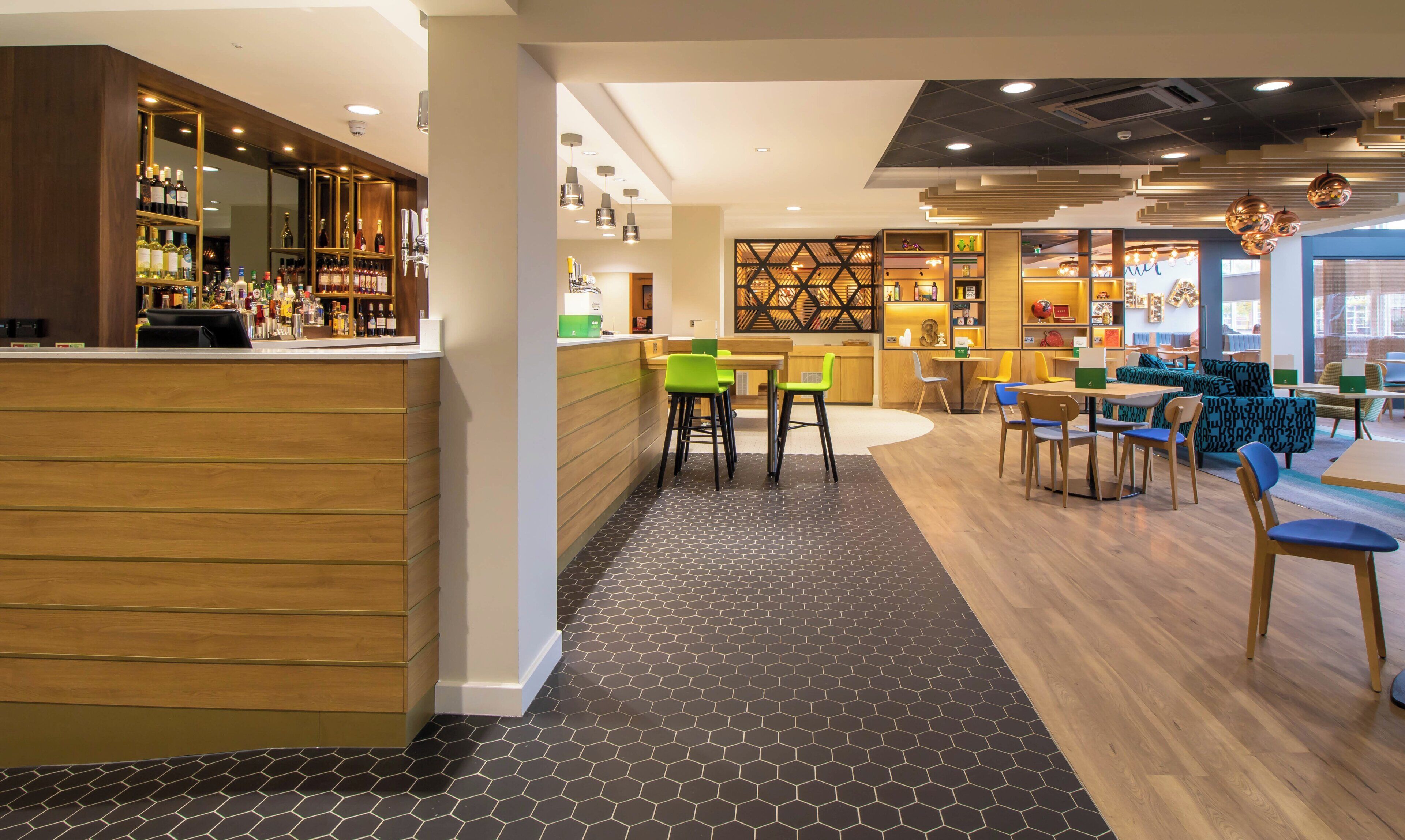 Uma área de bar com balcão de madeira e espaço para sentar com cadeiras coloridas.