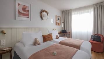 Quarto de hotel com duas camas, uma escrivaninha, uma cadeira e uma janela com cortinas.