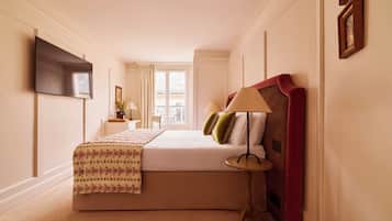 Quarto de hotel com uma cama, mesa de cabeceira, luminária, TV fixada na parede e janela com cortinas.