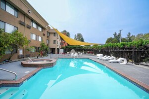 Piscina com espreguiçadeiras, toldo amarelo e um edifício com várias janelas e varandas.