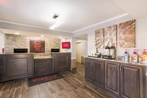 Uma área de recepção com parede de pedra, placa Red Roof Inn, televisão de tela plana e um espaço para café.