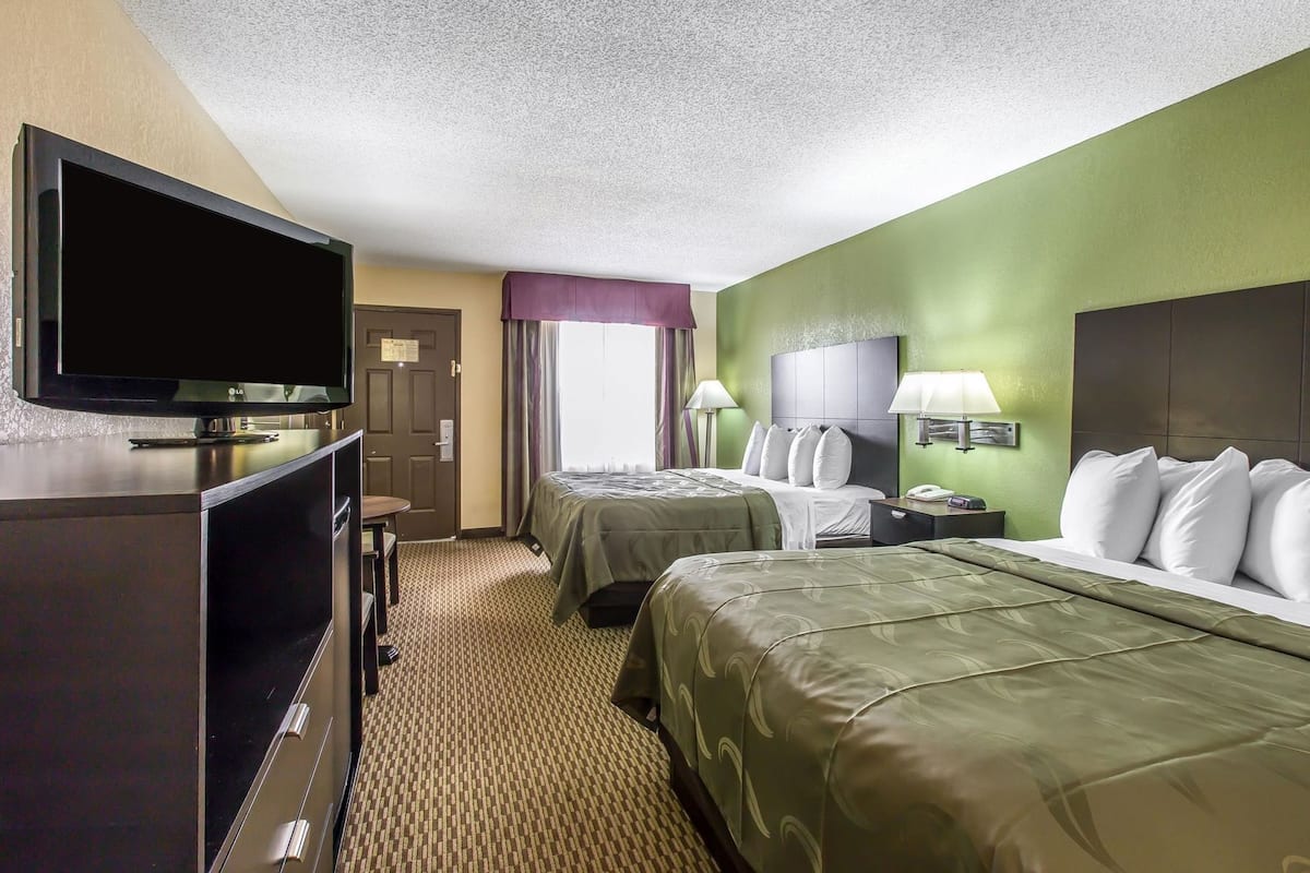 Quarto de hotel com duas camas, televisão, escrivaninha e abajur.