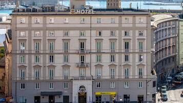 Um hotel com um destaque para a placa de B&B, uma loja PostaItaliane no andar térreo e vista para o porto no fundo.