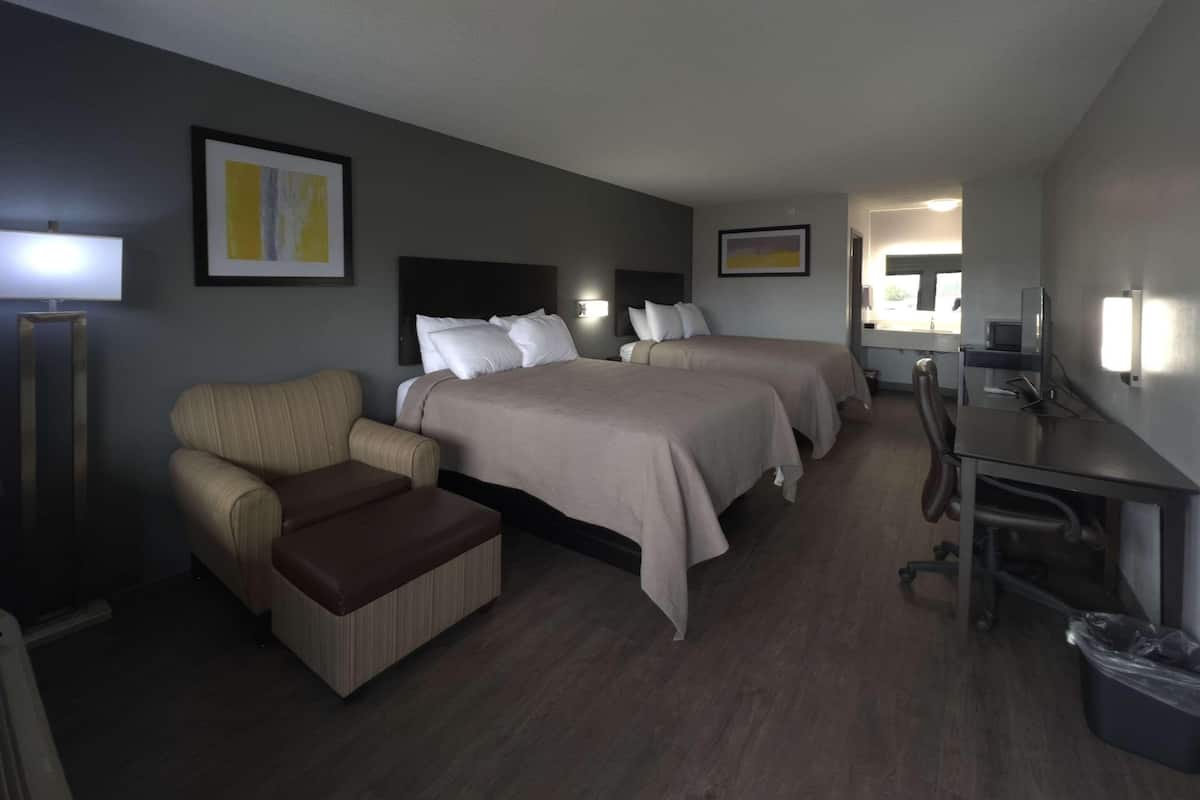 Quarto de hotel com duas camas, uma escrivaninha, uma cadeira, um abajur e uma lixeira.