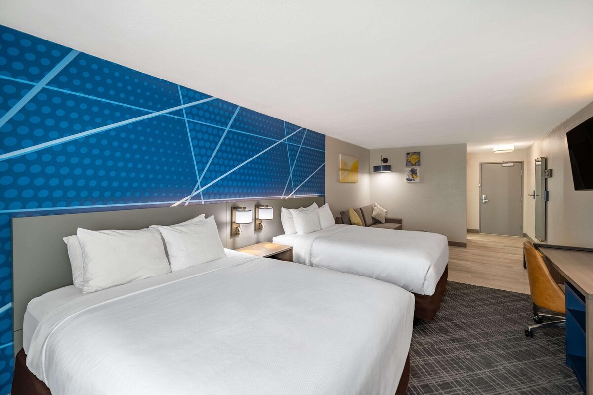 Quarto de hotel com duas camas, uma escrivaninha e uma televisão.