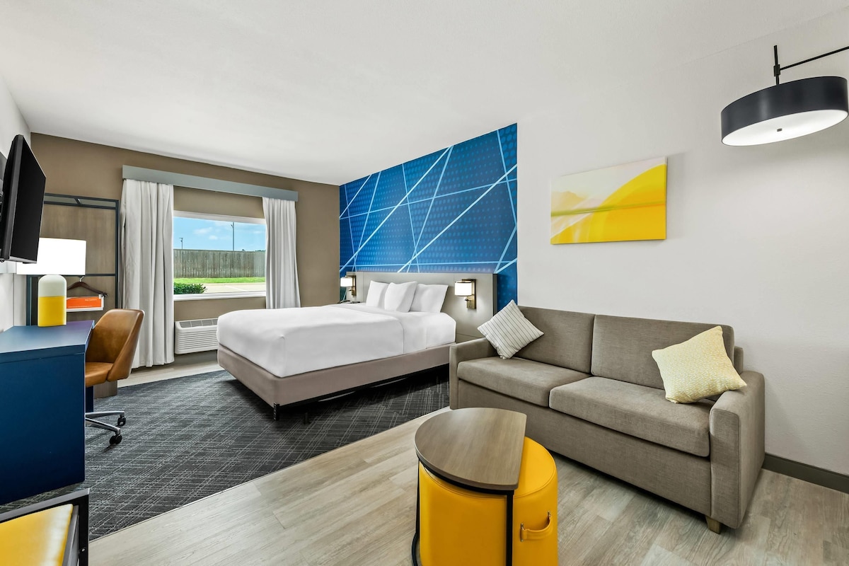 Quarto de hotel com cama, sofá, escrivaninha e televisão.