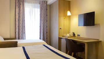 Quarto de hotel com duas camas, uma escrivaninha com cadeira, televisão de tela plana e janela com cortinas.