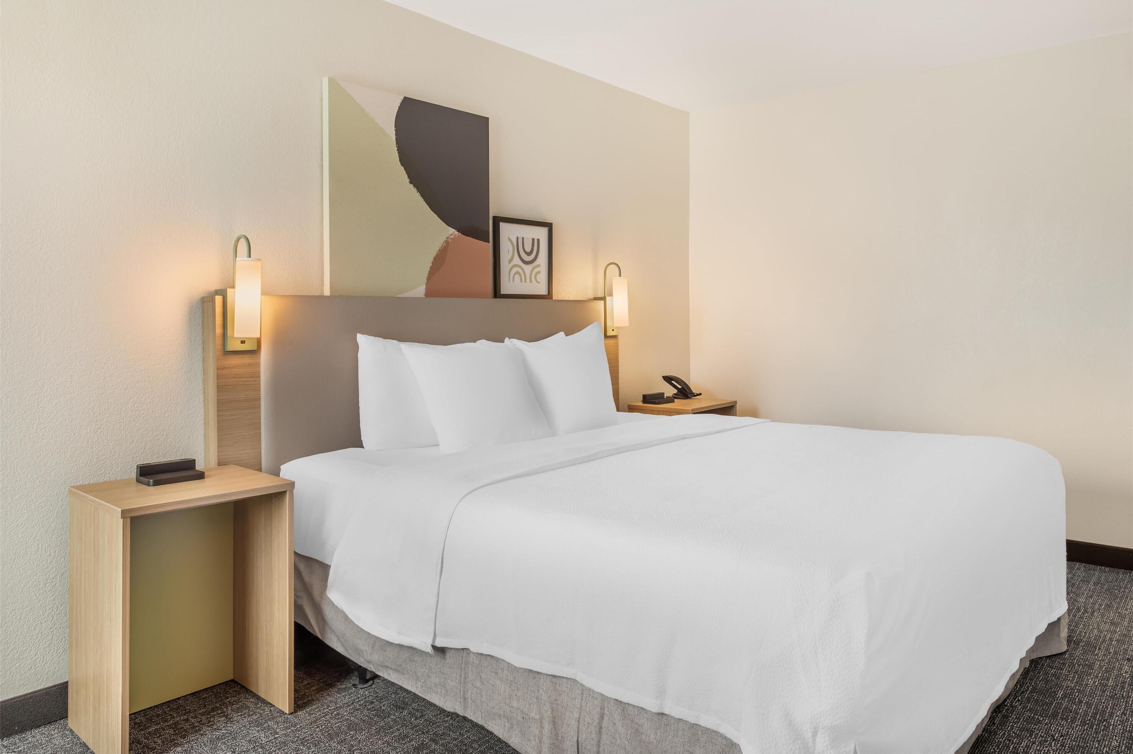 Quarto de hotel com cama, mesas de cabeceira e luminárias fixadas na parede.