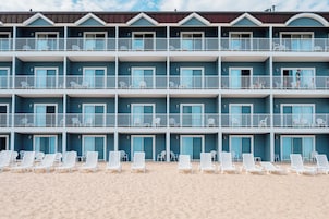 Um hotel com vários andares, varandas, cadeiras de praia e uma praia de areia.